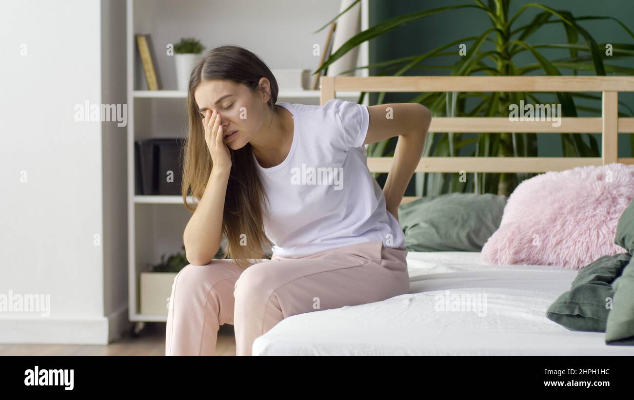 Young Woman Feels Back Pain on the Bed at Home, Rubs Her Lower Back ...