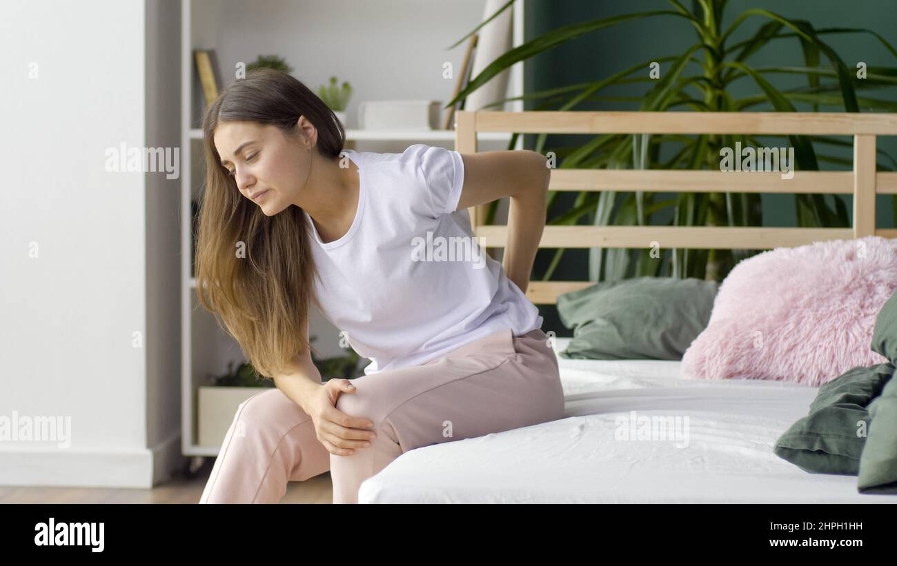 Young Woman Feels Back Pain on the Bed at Home, Rubs Her Lower Back ...