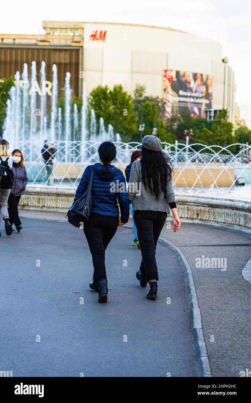Back view of two women walking on street and holding their hands in ...