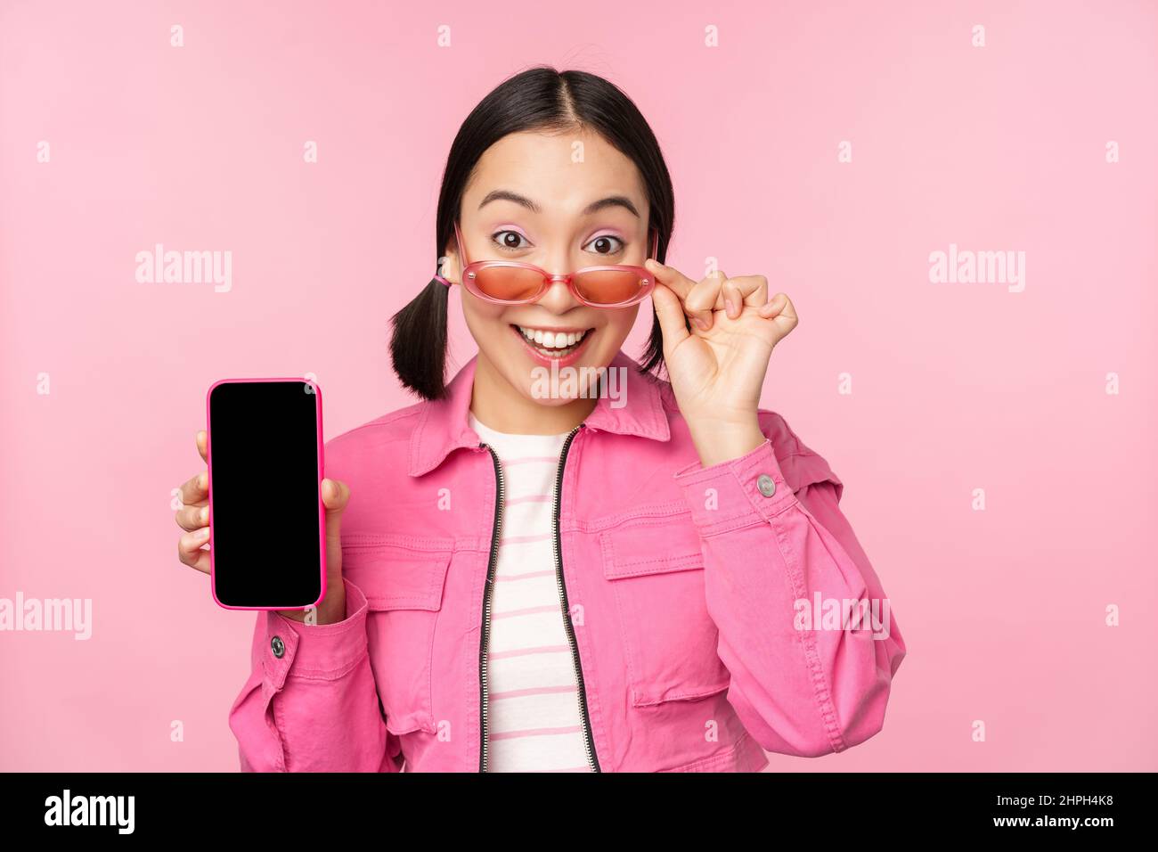 Portrait of asian girl showing mobile phone screen, reacting surprised ...