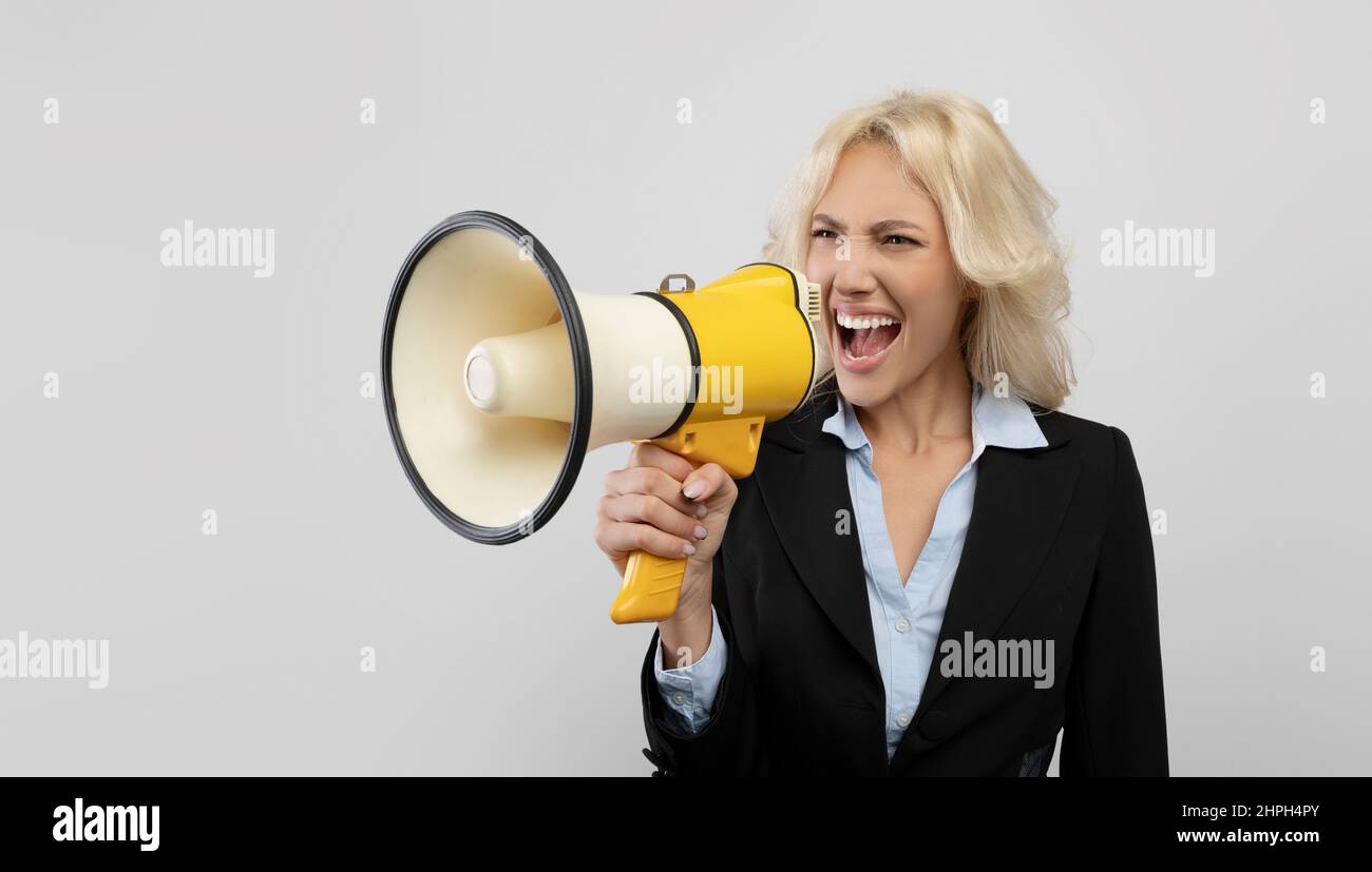 Irritated female office worker in formal wear screaming in megaphone ...