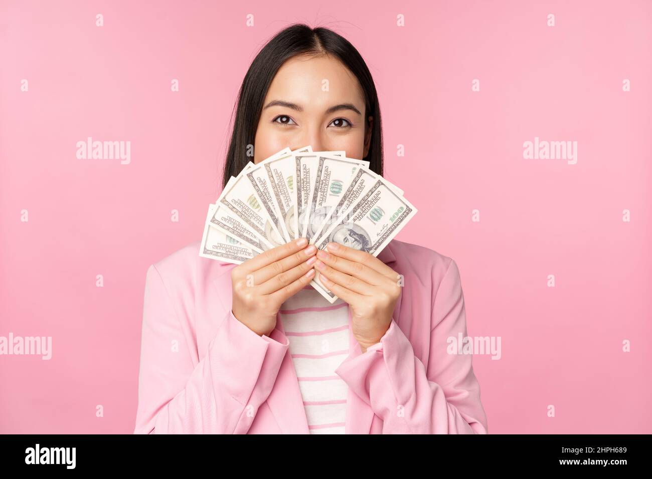 Happy asian lady in suit holding money, dollars with pleased face ...