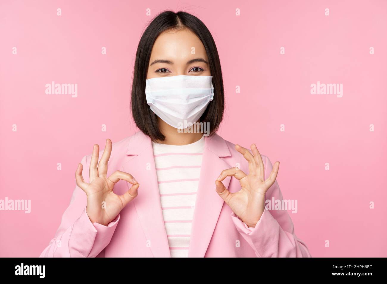 Asian businesswoman in suit and medical face mask, showing okay sign ...