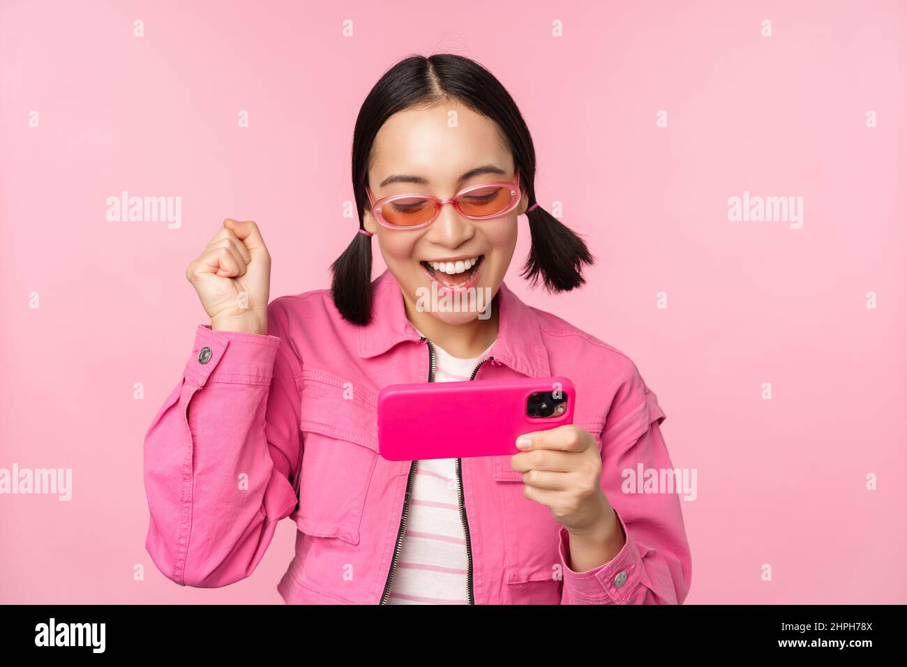 Happy smiling korean girl winning on mobile phone, looking at ...