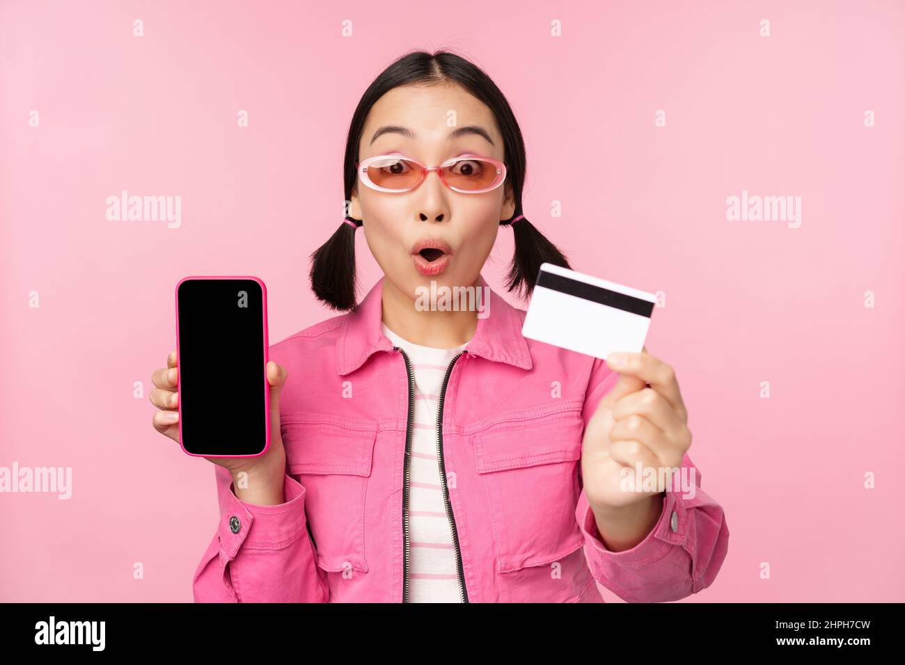 Asian girl shows mobile phone screen and credit card, reacts surprised ...