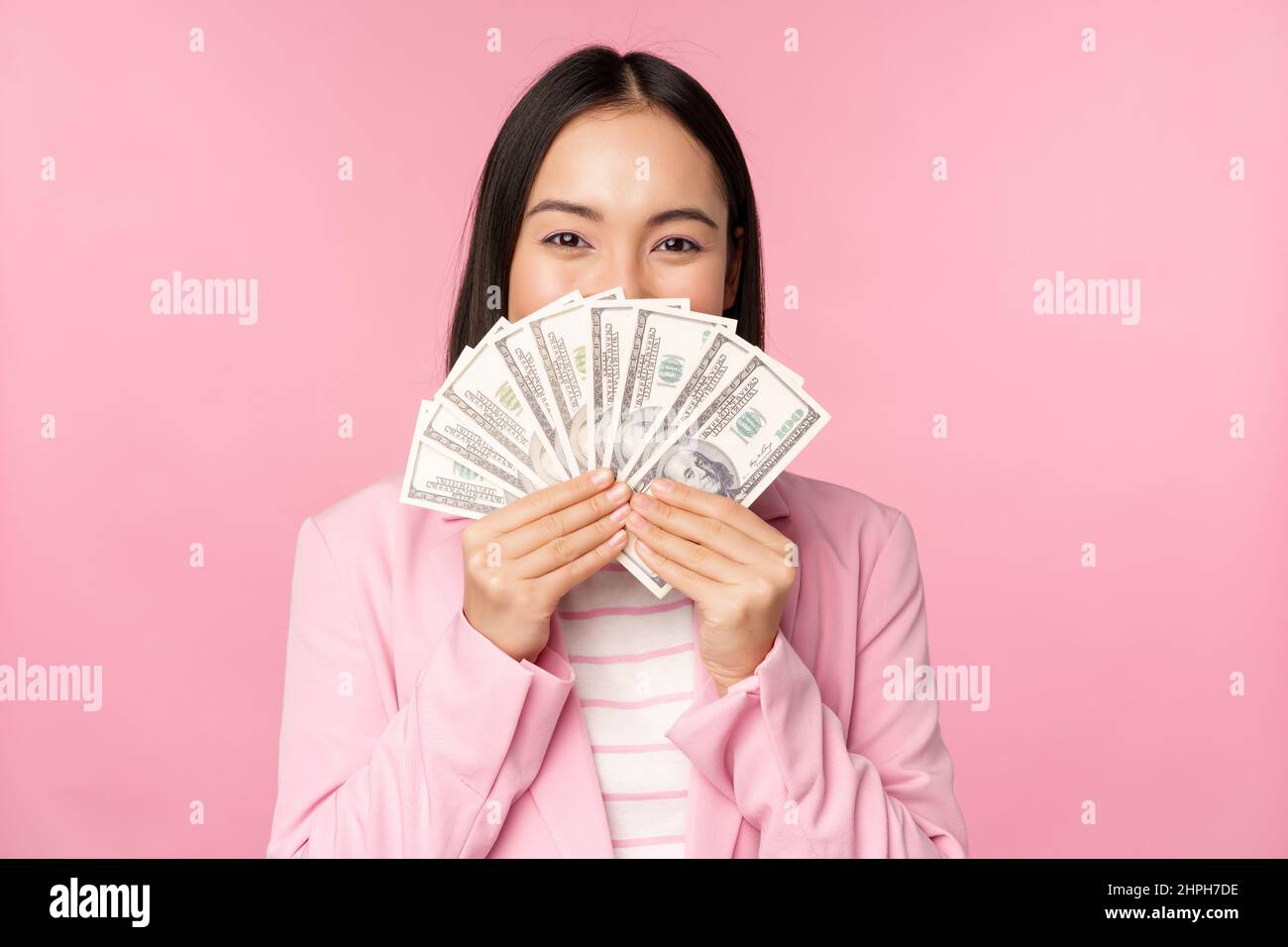Happy asian lady in suit holding money, dollars with pleased face ...