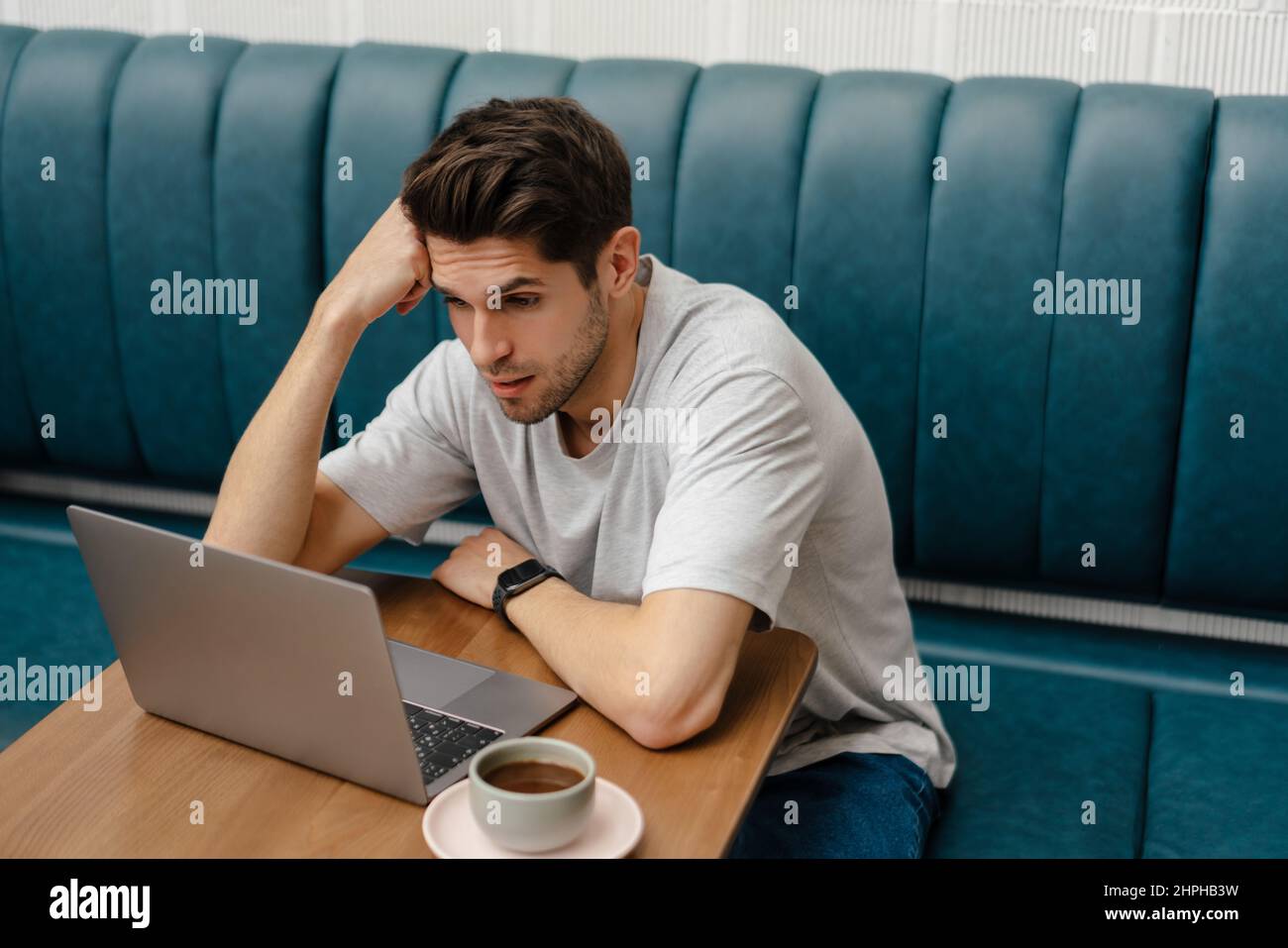 Confused young man student sitting in cafe indoors with laptop computer ...