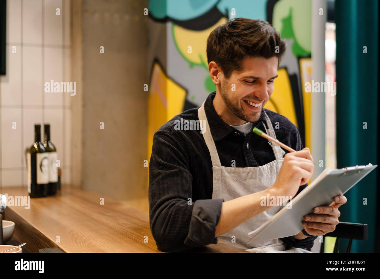 Smiling young waiter checking the quality of goods with notepad in ...