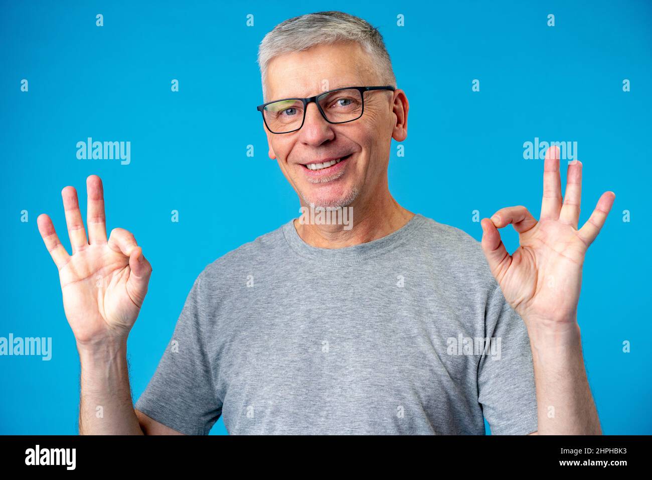 Happy positive handsome old man shows Ok sign over blue background ...