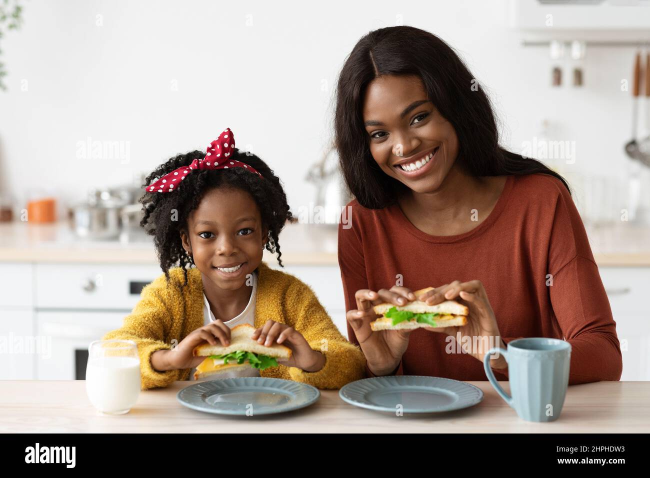 Portrait Of Happy Black Mother And Little Daughter Eating Sandwiches In Kitchen Stock Photo - Alamy