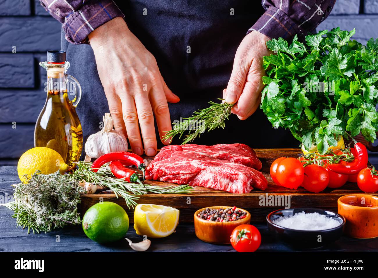 male chef is holding the fresh rosemary over the top of chuck eye beef ...