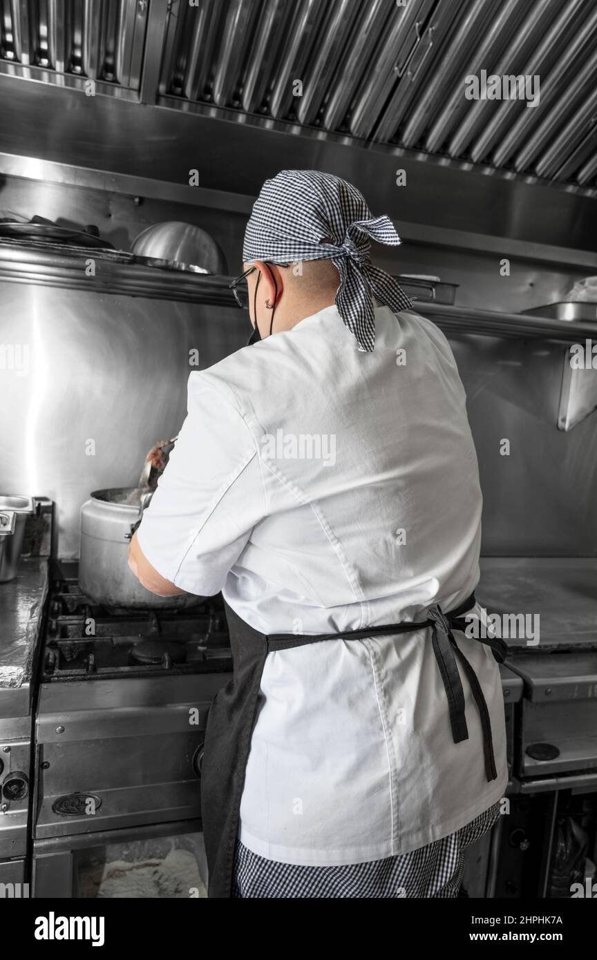 Back view of woman chef cooking food in the kitchen of a restaurant ...