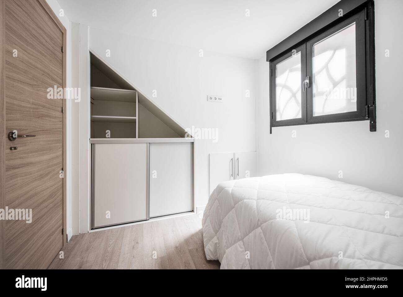 Room with a corner bed covered with a white quilted duvet, black ...