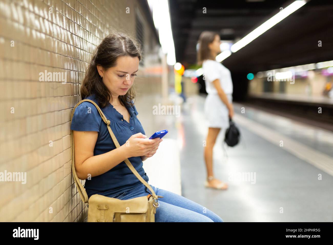 Woman with phone waiting at underground station Stock Photo - Alamy