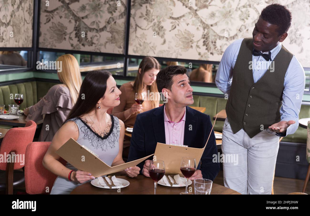 African American waiter recommending dishes from restaurant menu Stock ...