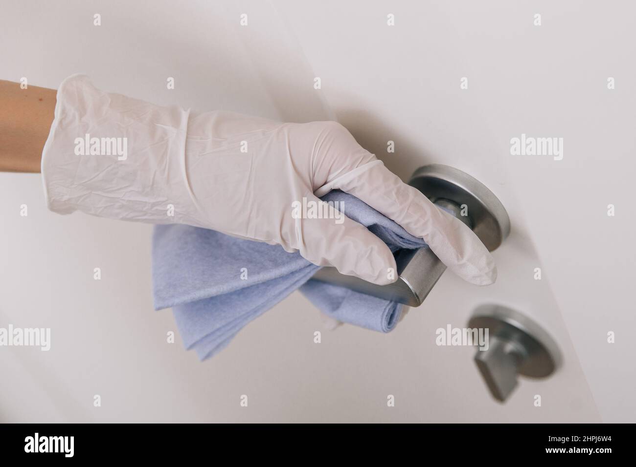 Cleaning door handle with blue wipe in white gloves. Sanitize surfaces ...