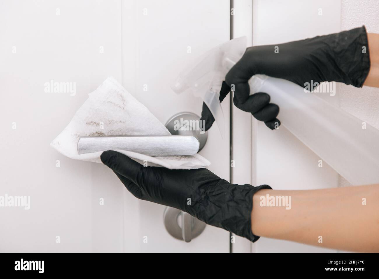 Cleaning door handle with dirty wipe in black gloves and sanitizer ...