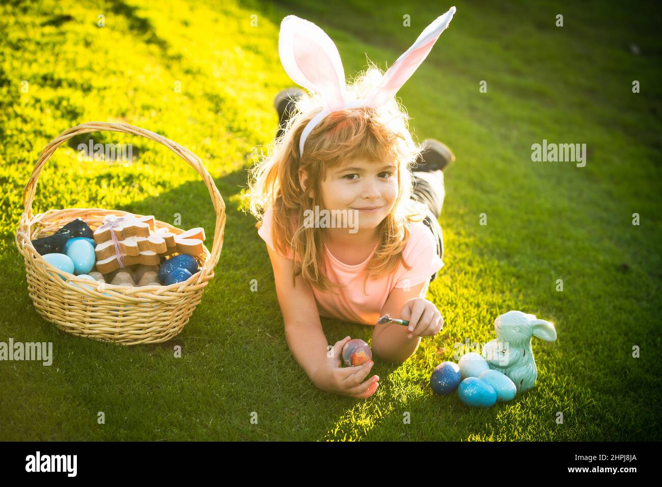 Child with easter eggs and bunny ears laying on grass. Funny boy ...