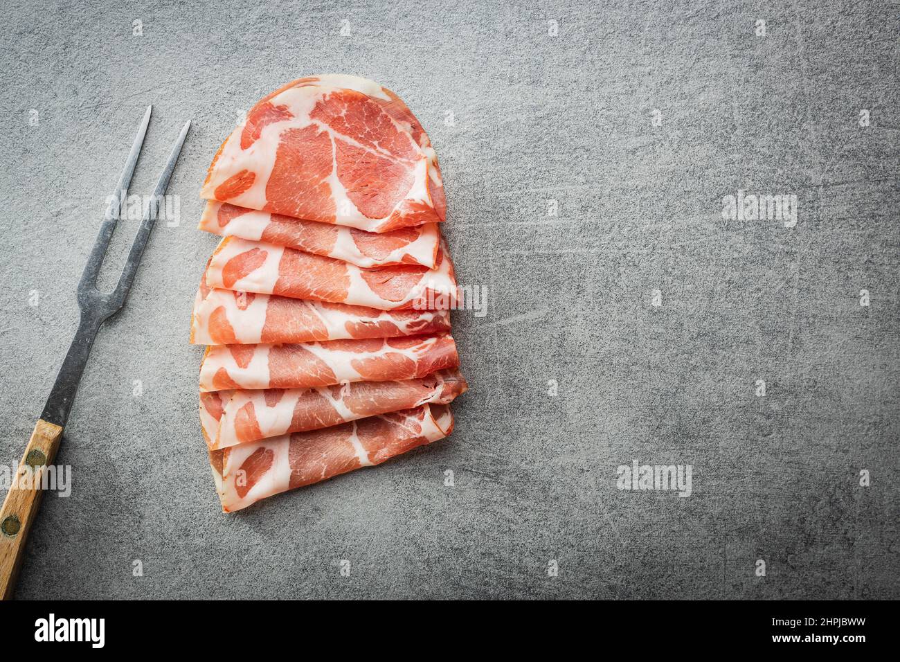 Italian dried ham. Coppa Stagionata with fork on a kitchen table. Top ...