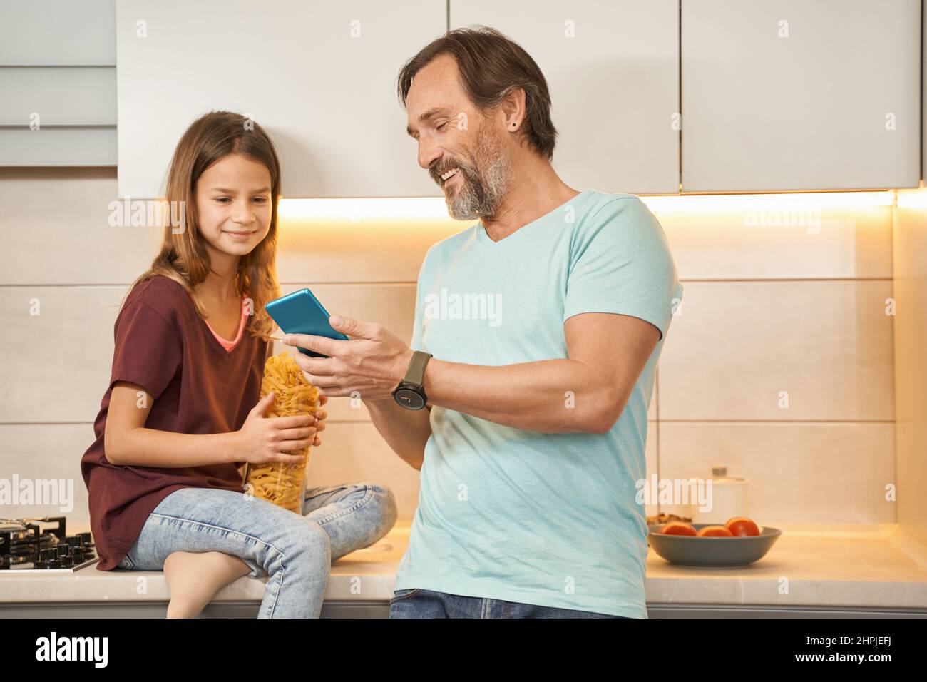 Adult man with a teenage girl in the kitchen watching a smartphone ...
