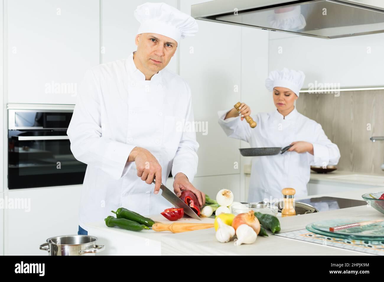 Two positive female and male young cooks wearing uniform working Stock ...