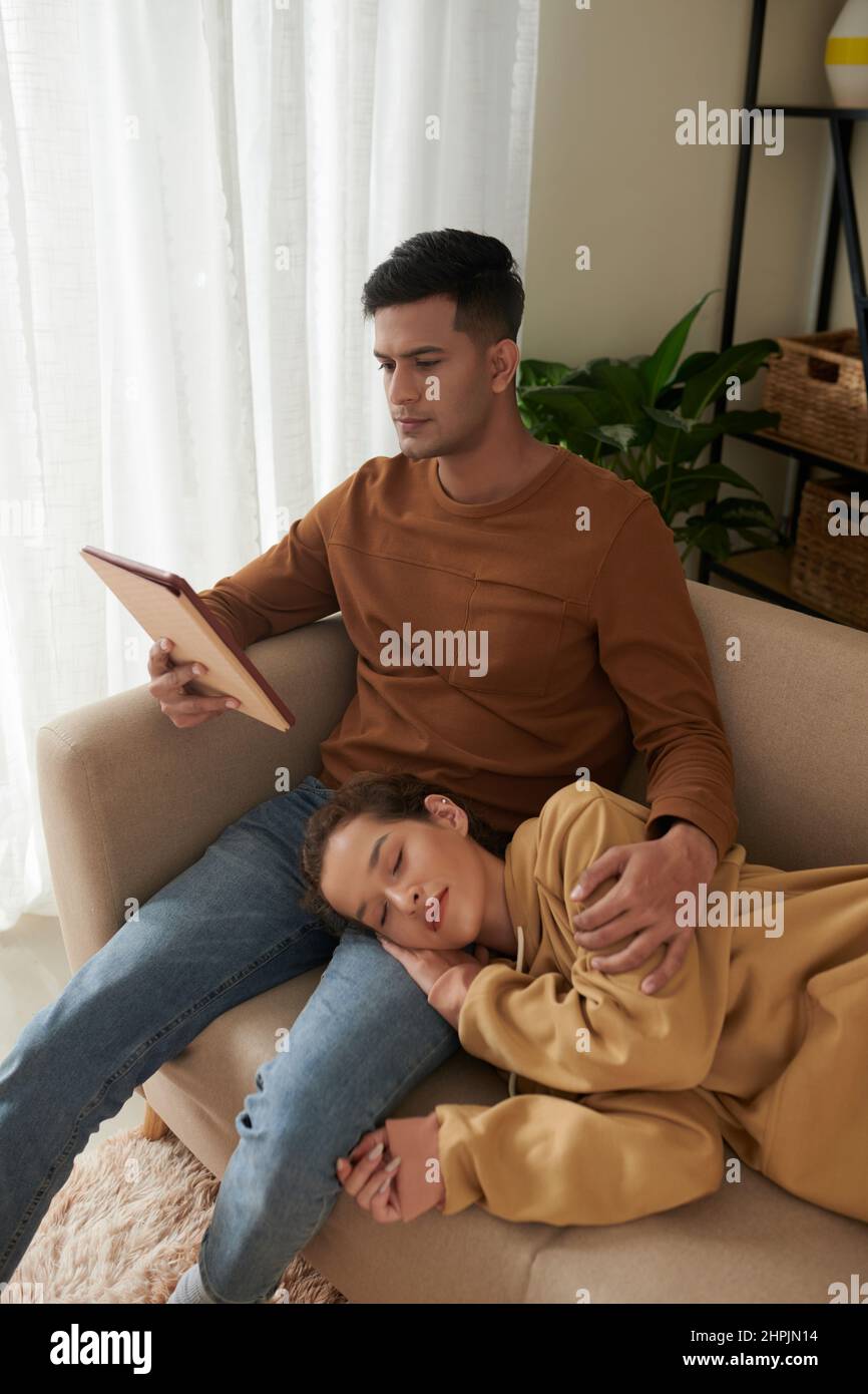 Young man watching something on tablet pc while resting on sofa with ...