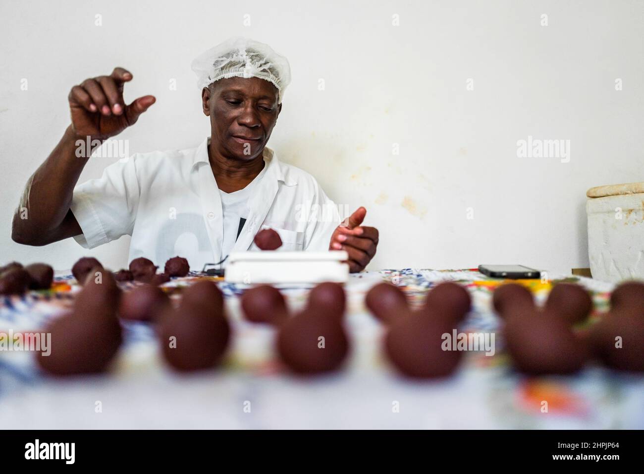 An Afro-Colombian farmer, rolls the raw cacao paste with hands into ...