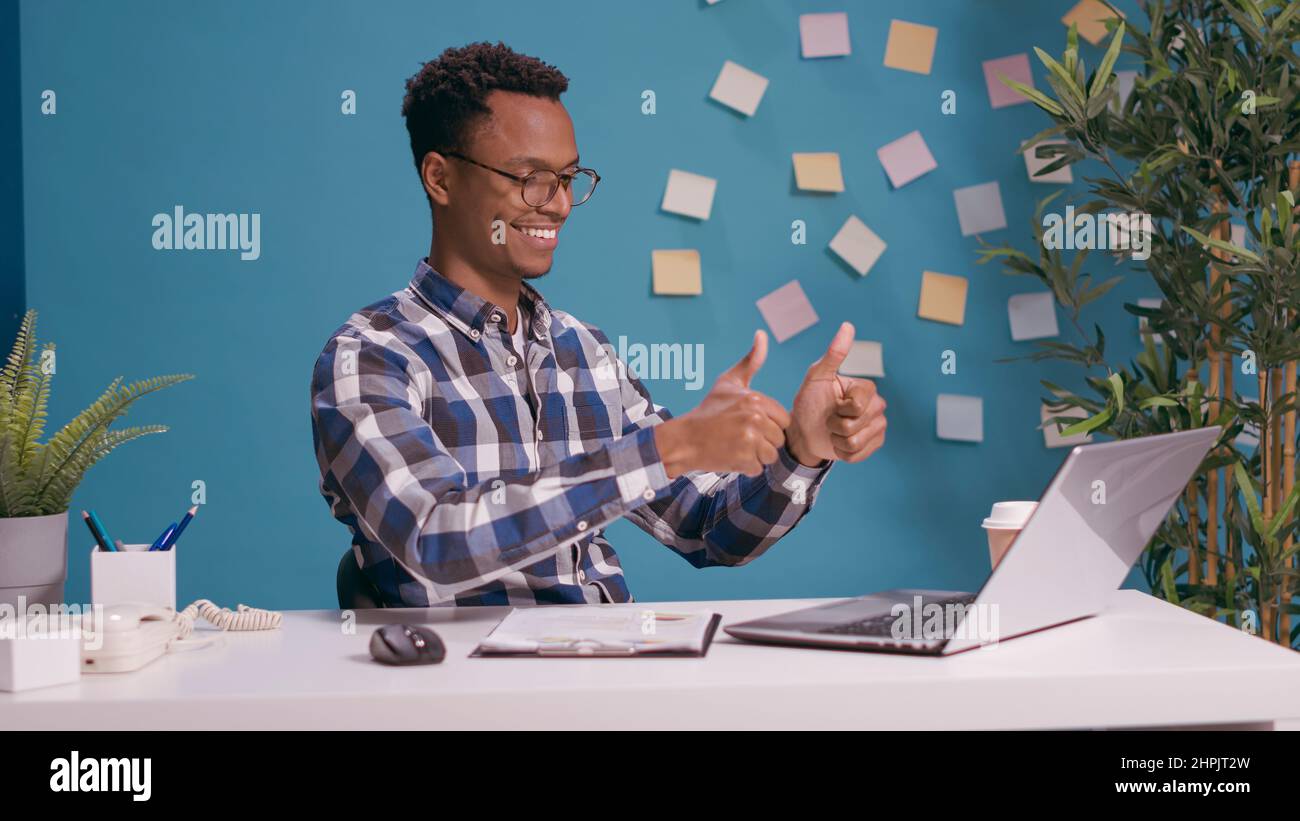 Cheerful person showing thumbs up gesture in front of laptop screen ...
