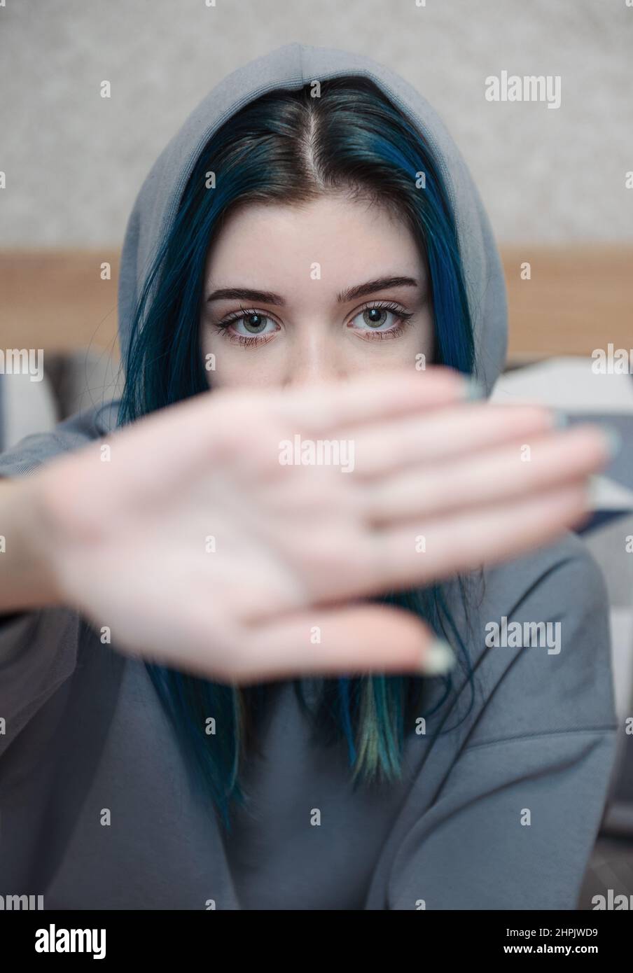 A teenage girl with blue hair covers her face with her hand. Teenage ...