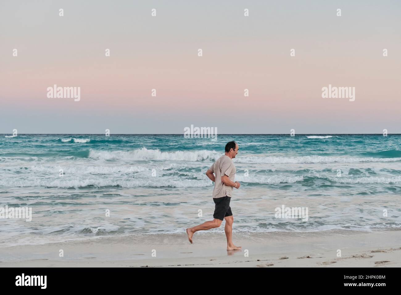 Senior asian man running barefoot on sandy ocean beach at sunrise Stock ...