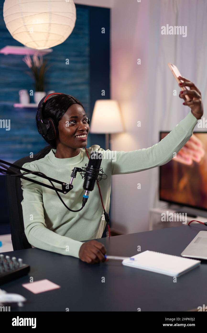 Vlogger woman with headphones smiling while taking selfie using modern ...