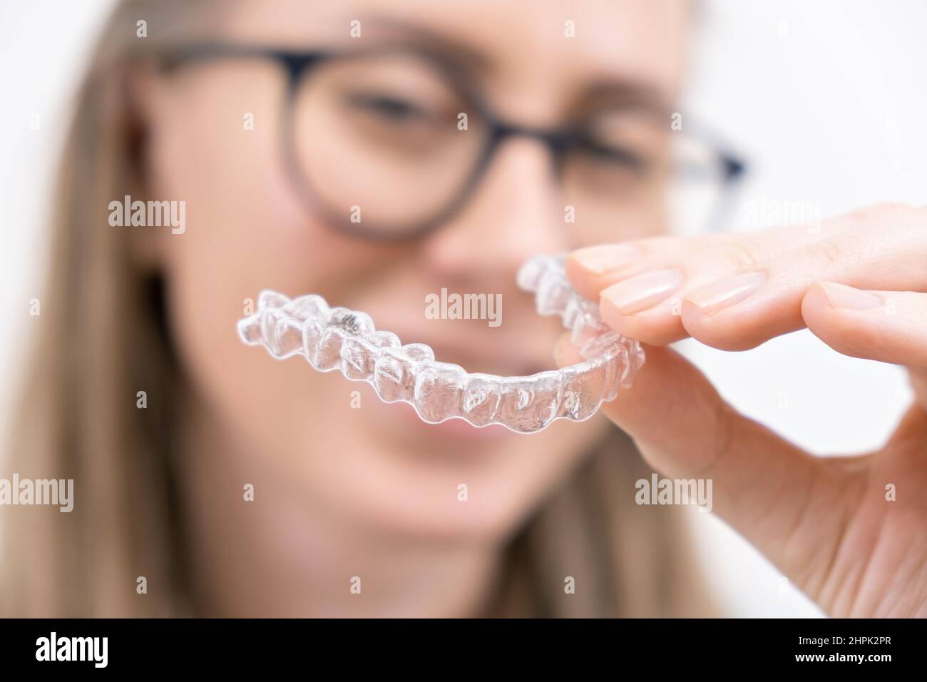 smiling woman using clear plastic removable braces aligner or whitening ...