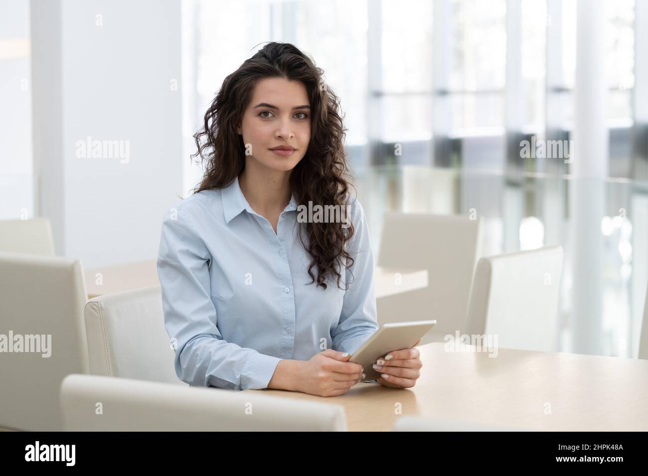 Young confident female ceo with digital tablet sitting by workplace and ...