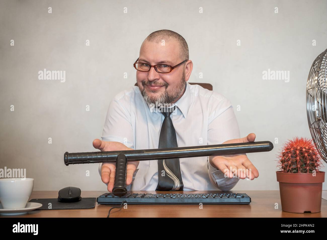 A smiling businessman sitting behind a desk politely offers a baton ...