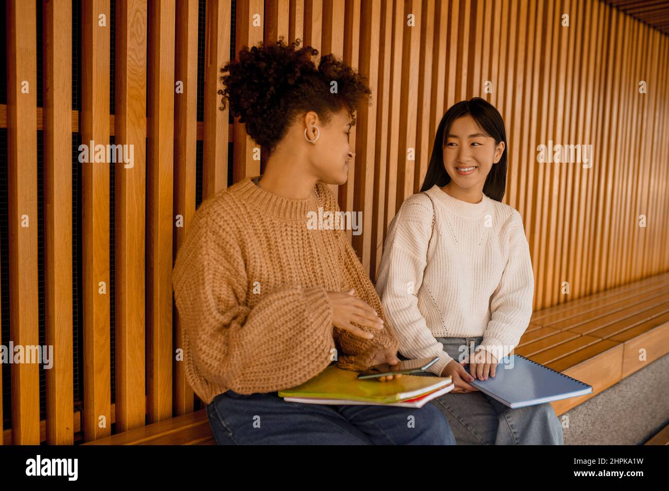 Two girls sitting on a bench and talking Stock Photo - Alamy
