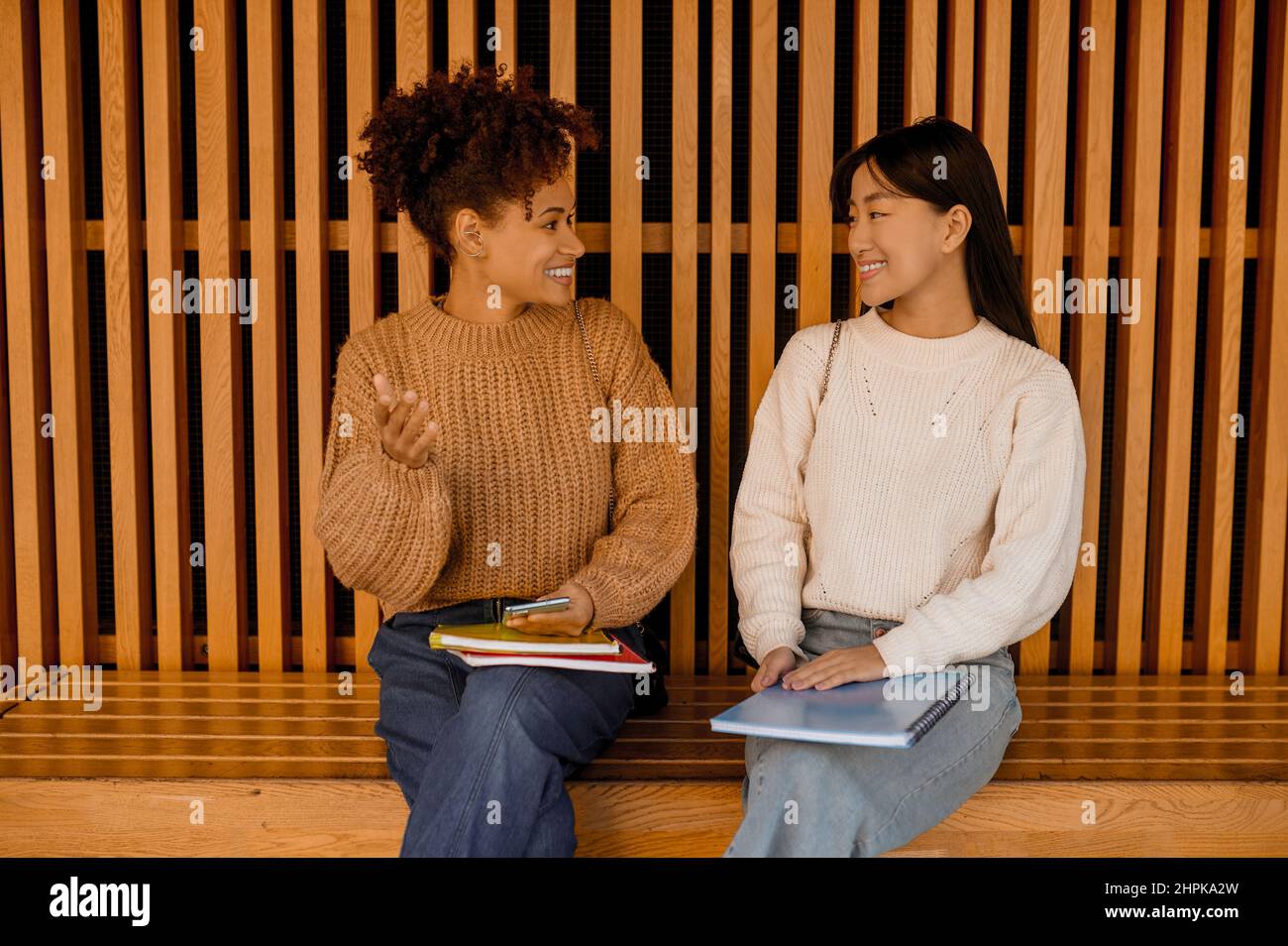 Two girls sitting on a bench and talking Stock Photo - Alamy