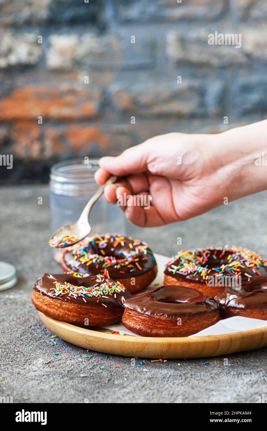 Fried doughnuts with chocolate glaze. Woman's hand decorating doughnuts ...