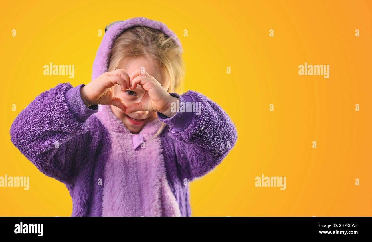 little girl in purple pajamas making heart shape by hand on yellow ...