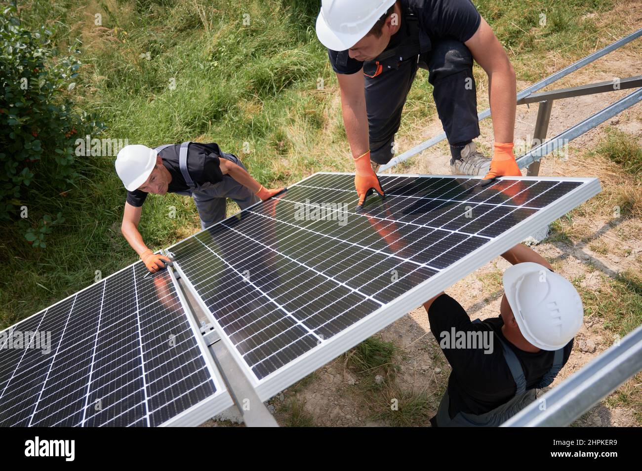 Workers installing solar panel on metal beams in field at sunny daytime ...