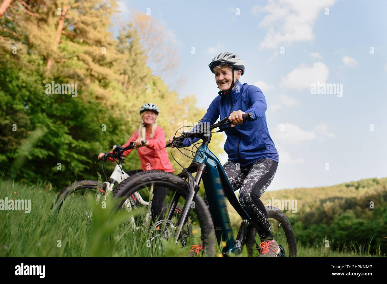 Happy active senior women friends cycling together outdoors in nature ...