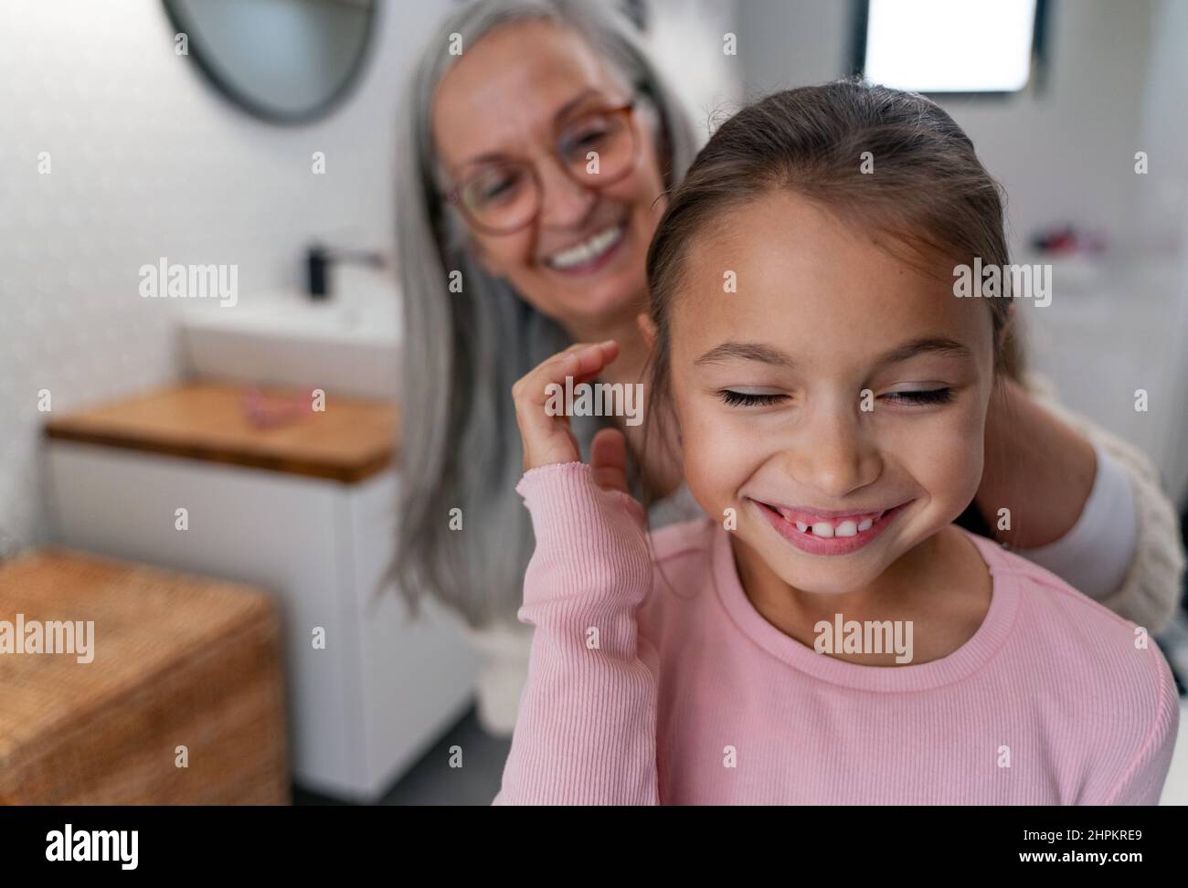 Happy senior grandmother and granddaughter standing indoors in bathroom ...