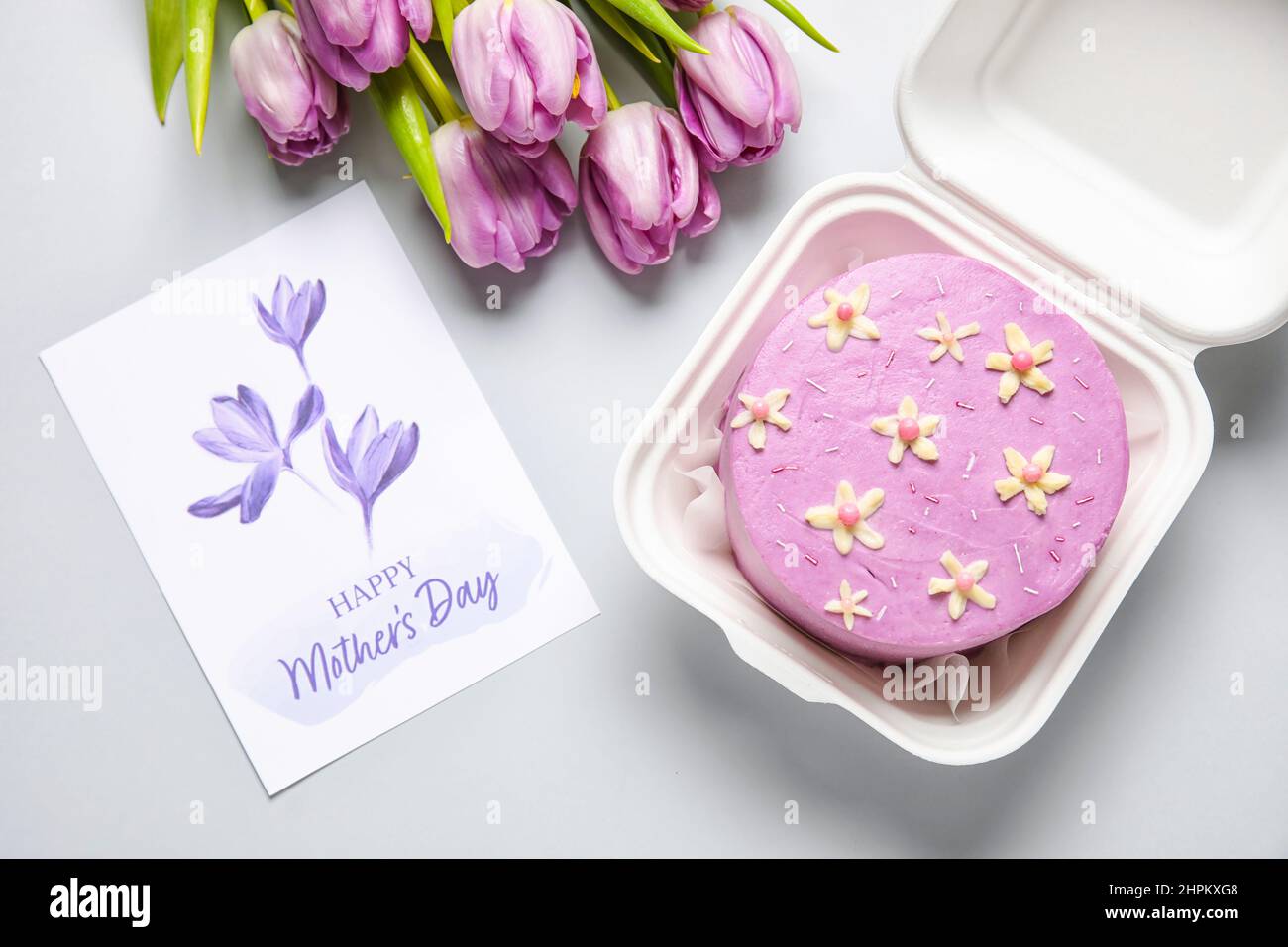 Plastic lunch box with tasty bento cake, greeting card and flowers on ...