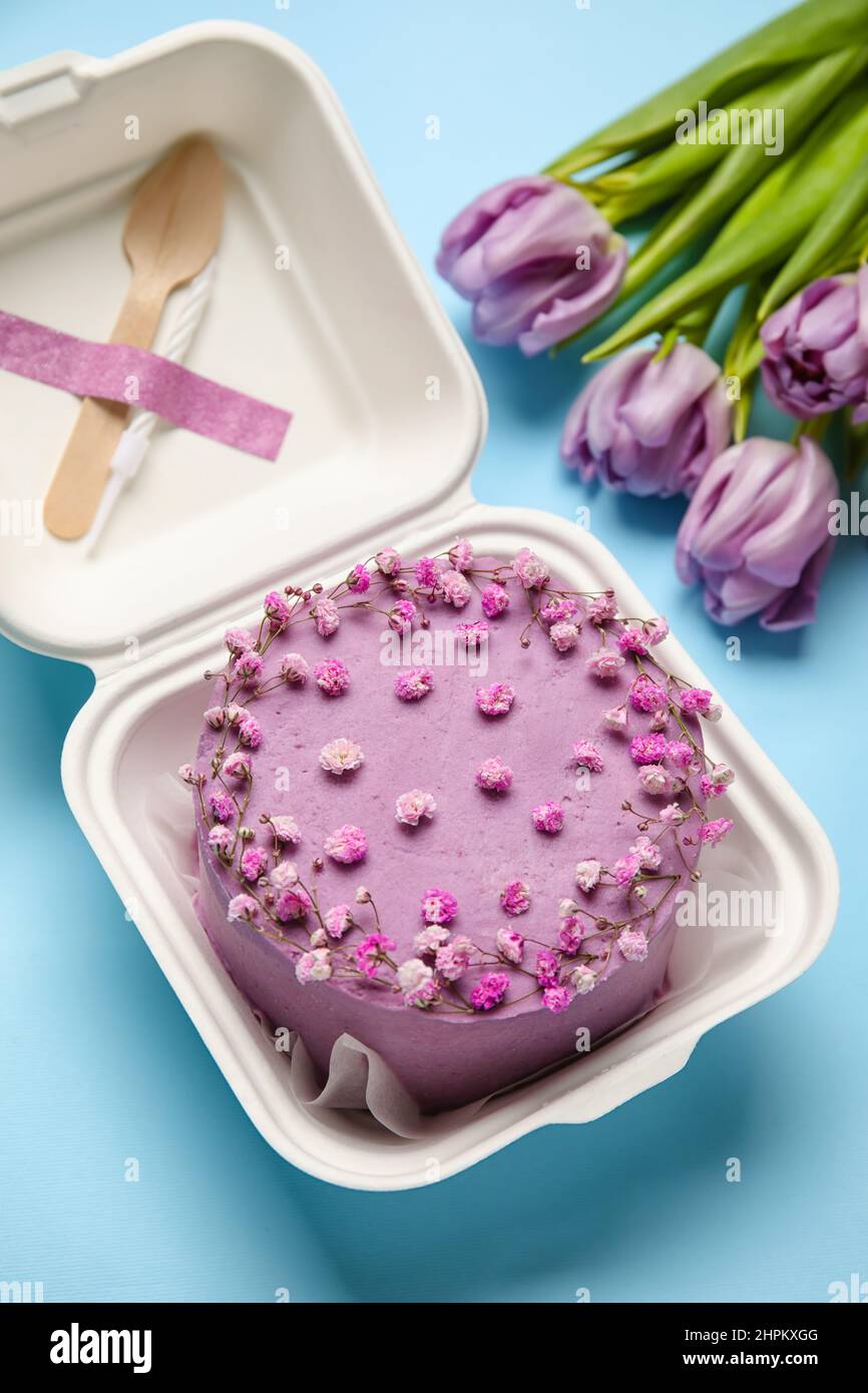 Plastic lunch box with tasty bento cake and flowers on blue background ...
