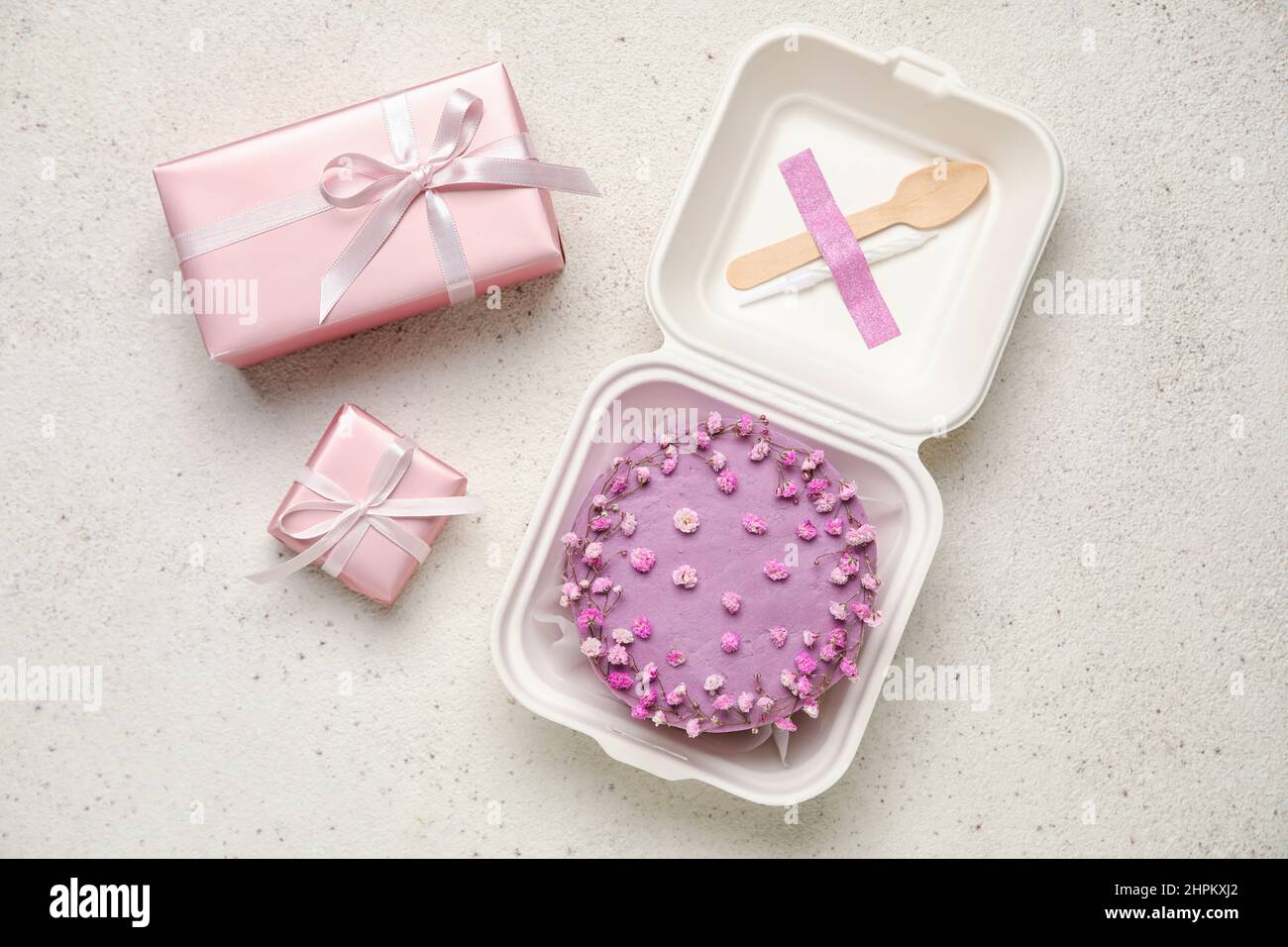 Plastic lunch box with tasty bento cake and gifts on light background ...