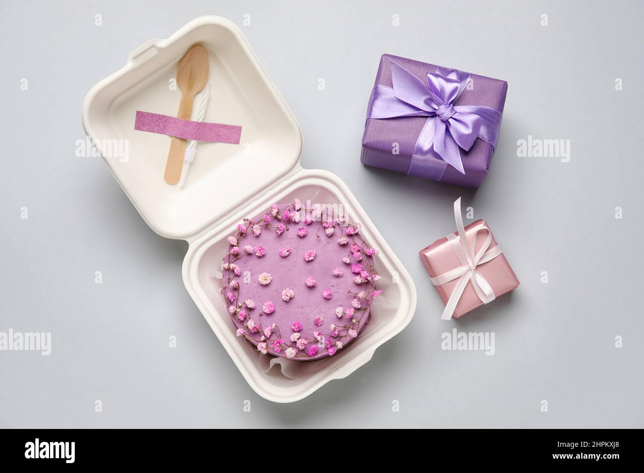 Plastic lunch box with tasty bento cake and gifts on grey background ...