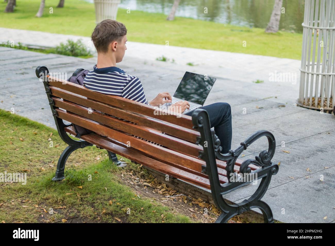 Young caucasian man sitting on the bench in the park and working on the ...