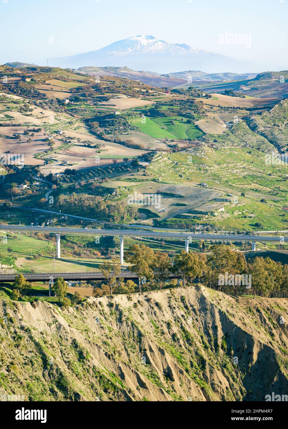 Eroded badlands and cultivated hills with outline of Mount Etna volcano ...