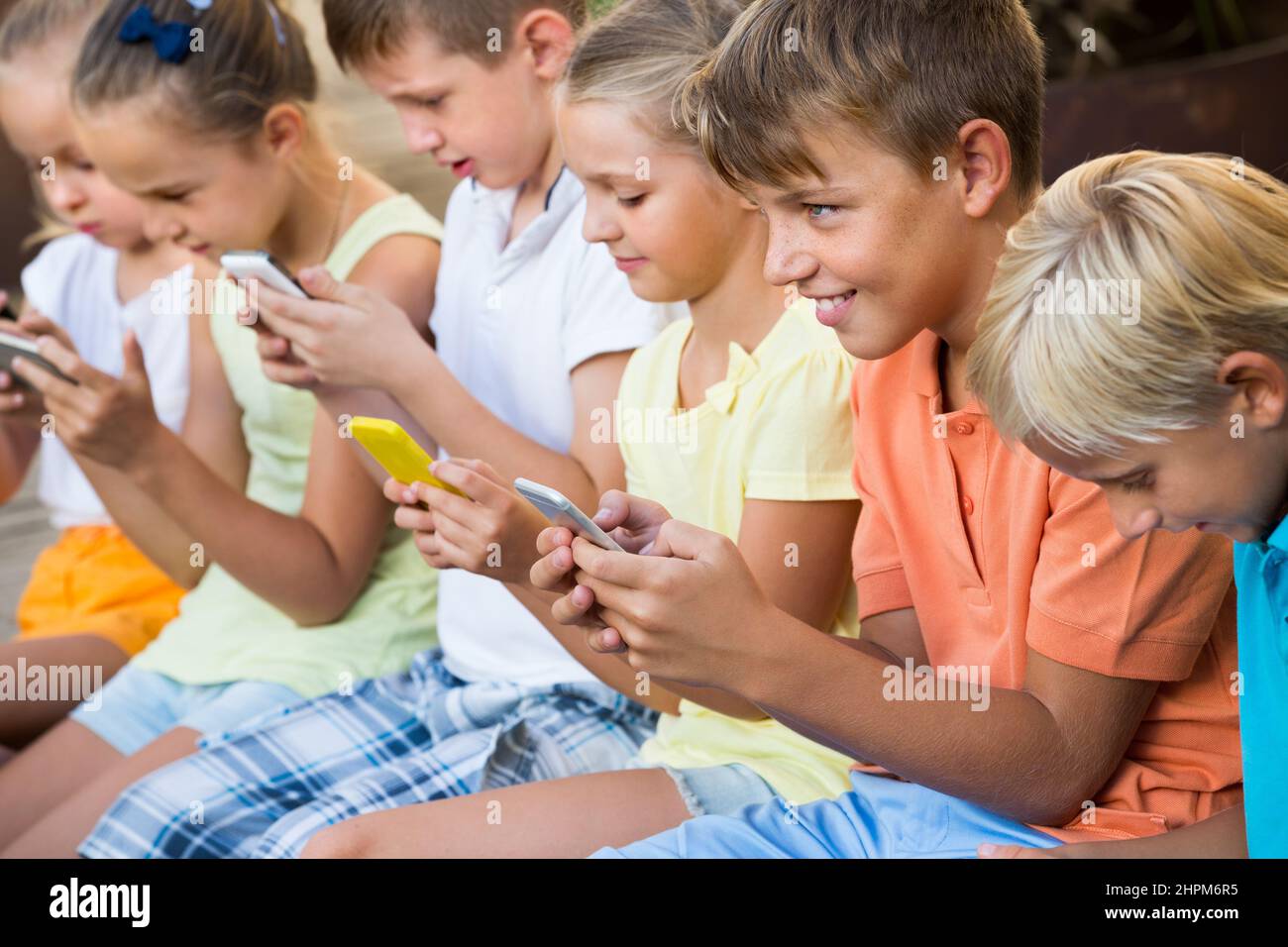 Group of positive kids playing with mobile phones outdoors Stock Photo ...