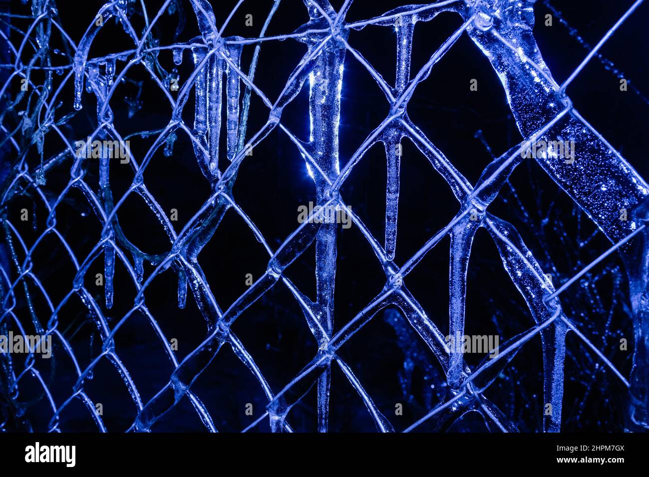 Photo of blue toned frozen metal fence covered in ice on dark ...