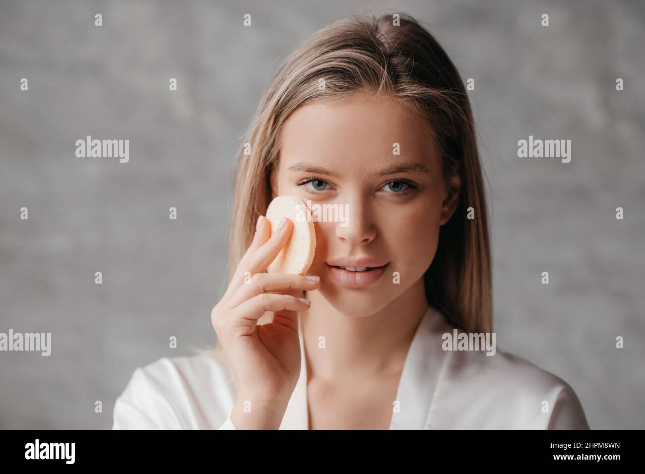 Skincare concept. Young woman using cosmetic sponge while doing facial ...